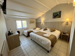 Quarto de hotel com duas camas, uma escrivaninha, uma cadeira, uma janela e um quadro na parede.
