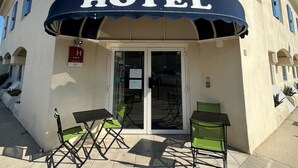 Um hotel chamado "LES ARCADES" com uma grande placa, área de estar ao ar livre e entrada por porta de vidro.