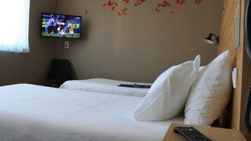 Quarto de hotel com duas camas, uma televisão presa à parede e um controle remoto no criado-mudo.