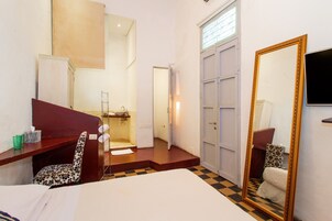 Quarto de hotel com uma cama, uma escrivaninha, uma cadeira, um espelho e um banheiro com pia e vaso sanitário.
