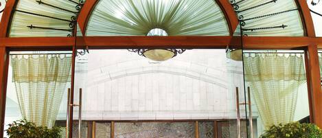 Um hall com uma grande entrada de vidro em arco, piso ladrilhado e duas plantas em vasos.