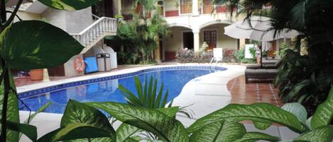 Piscina rodeada por vegetação exuberante e um edifício com vários andares e varandas.