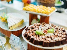Buffet com diversos doces, incluindo um bolo de chocolate com cobertura branca e folhas verdes.