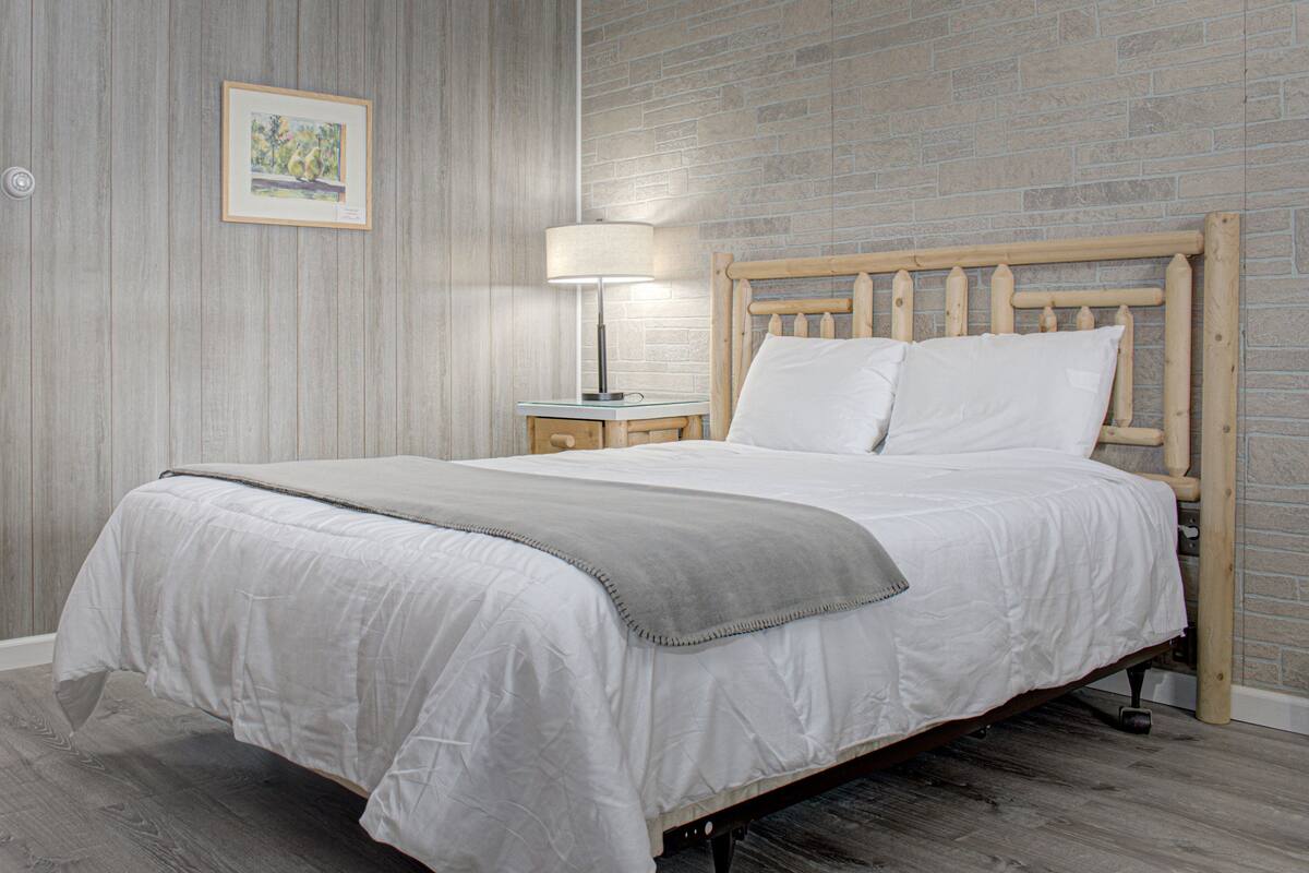 Uma cama bem arrumada com cabeceira de madeira, luminária de cabeceira e um quadro na parede.