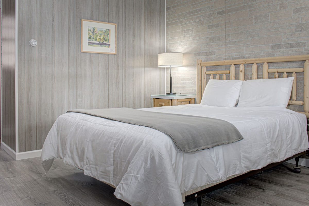 Quarto com cabeceira de madeira, mesa de cabeceira com abajur e quadro pendurado na parede.