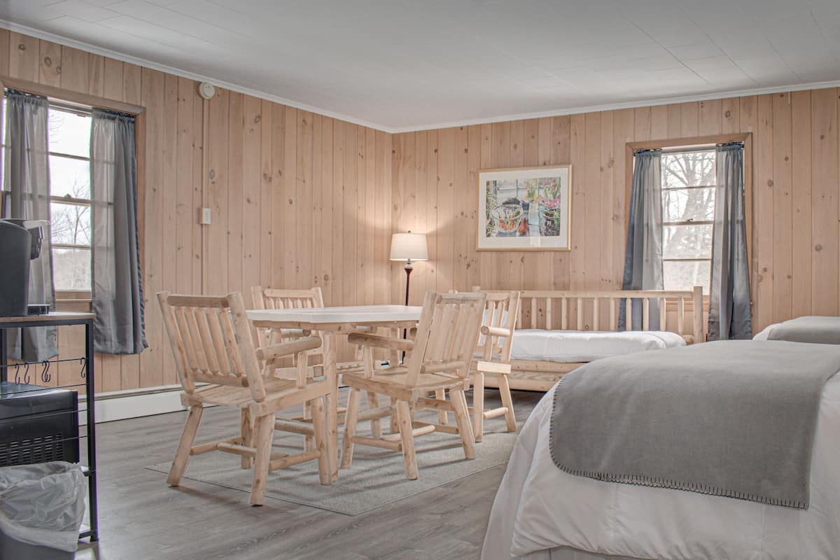 Quarto com paredes de madeira, uma mesa de jantar com cadeiras, uma cama e um quadro na parede.