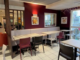Interior de restaurante com cabines e mesas, uma parede de destaque vermelha e uma janela com vista.