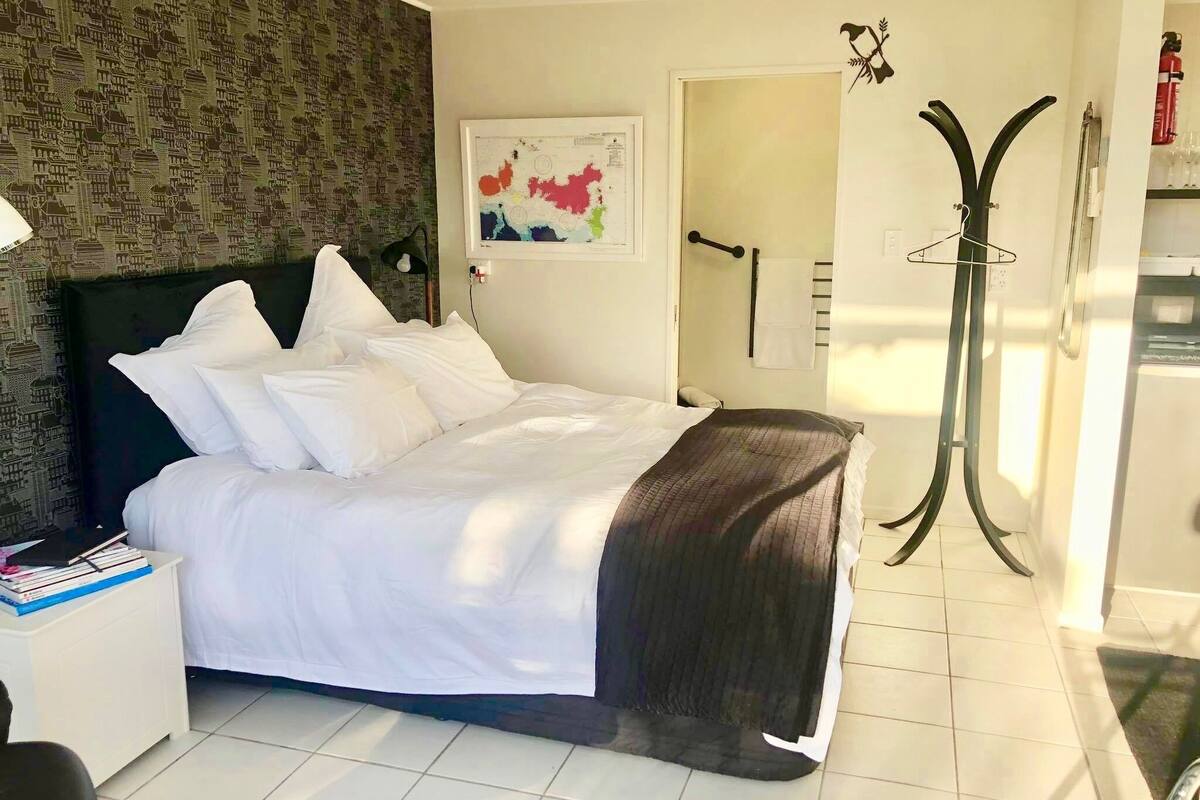 Uma cama bem arrumada com lençóis brancos, uma cabeceira preta e um mapa na parede.