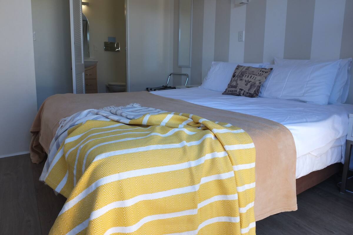 Quarto de hotel com cama, mesa de cabeceira, luminária e porta para um banheiro.