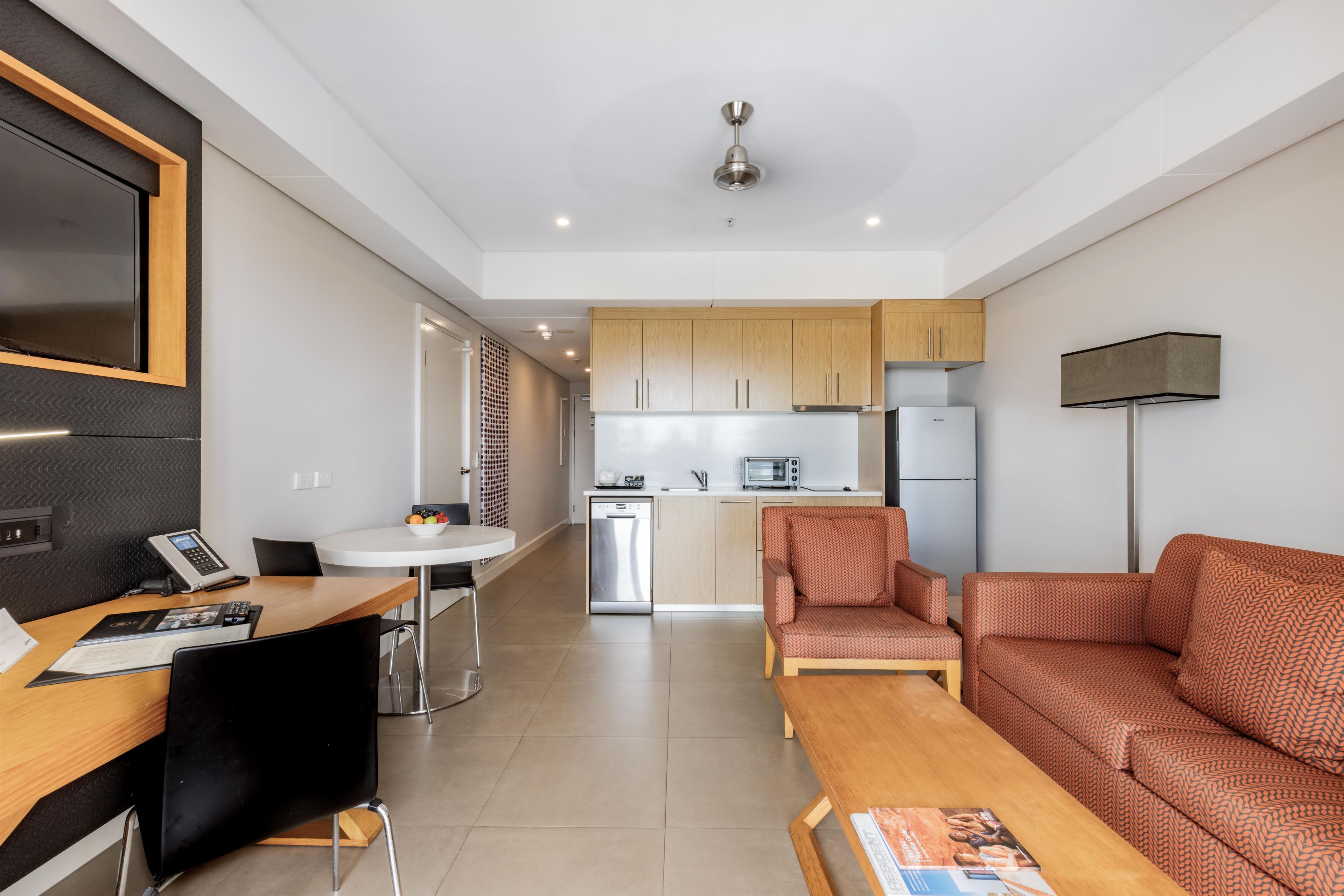 Uma sala de estar moderna com sofá, mesa de jantar e área de cozinha com armários e eletrodomésticos de madeira.