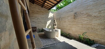 Uma área de spa com uma banheira de pedra grande, uma estátua e uma escada de bambu.