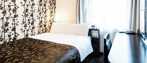 Quarto de hotel com cama, escrivaninha, cadeira, mesa de cabeceira com telefone e janela com cortinas.