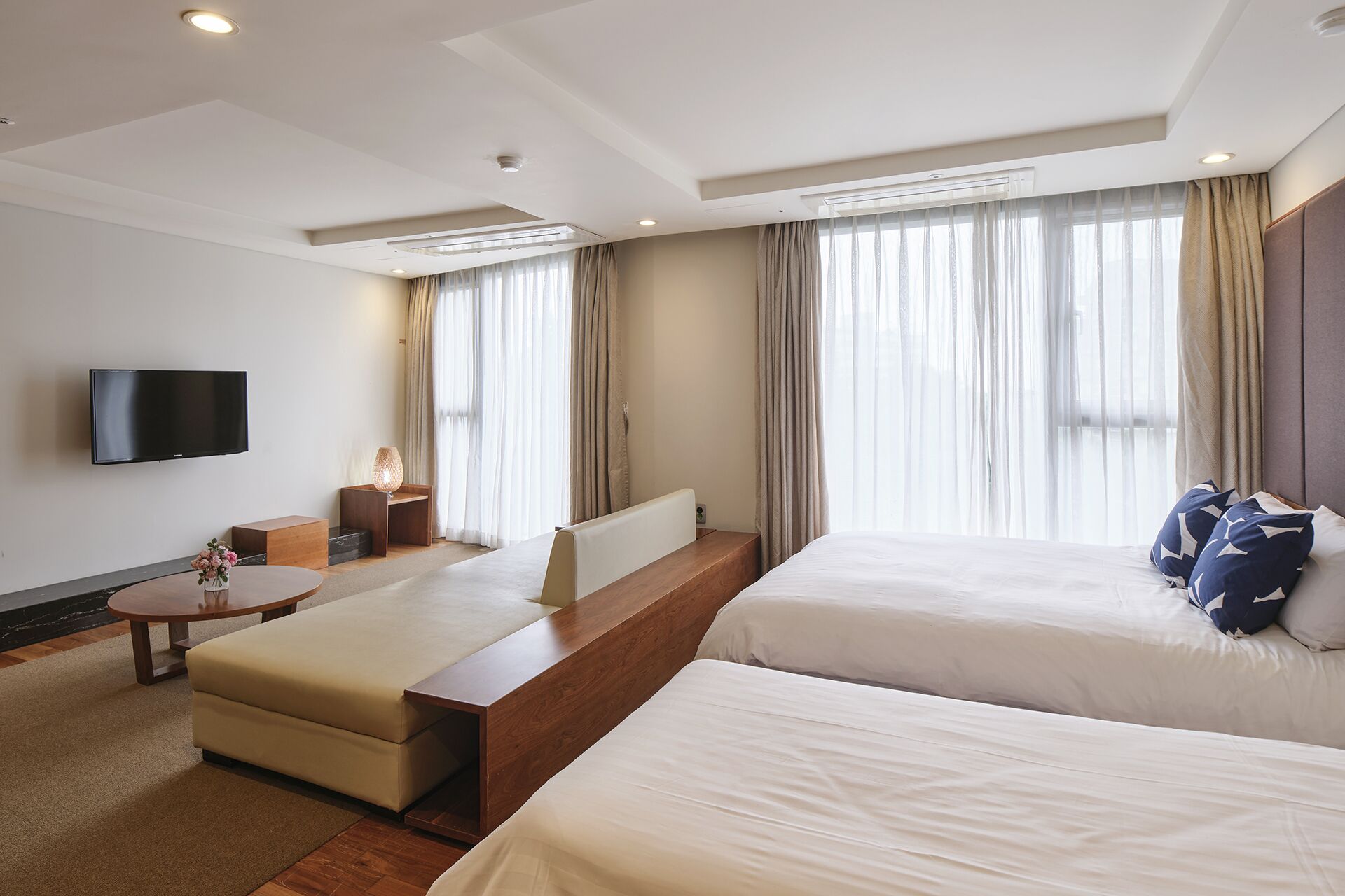 Quarto de hotel com duas camas, televisão, escrivaninha e sofá.