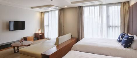 Quarto de hotel com duas camas, televisão, escrivaninha e sofá.