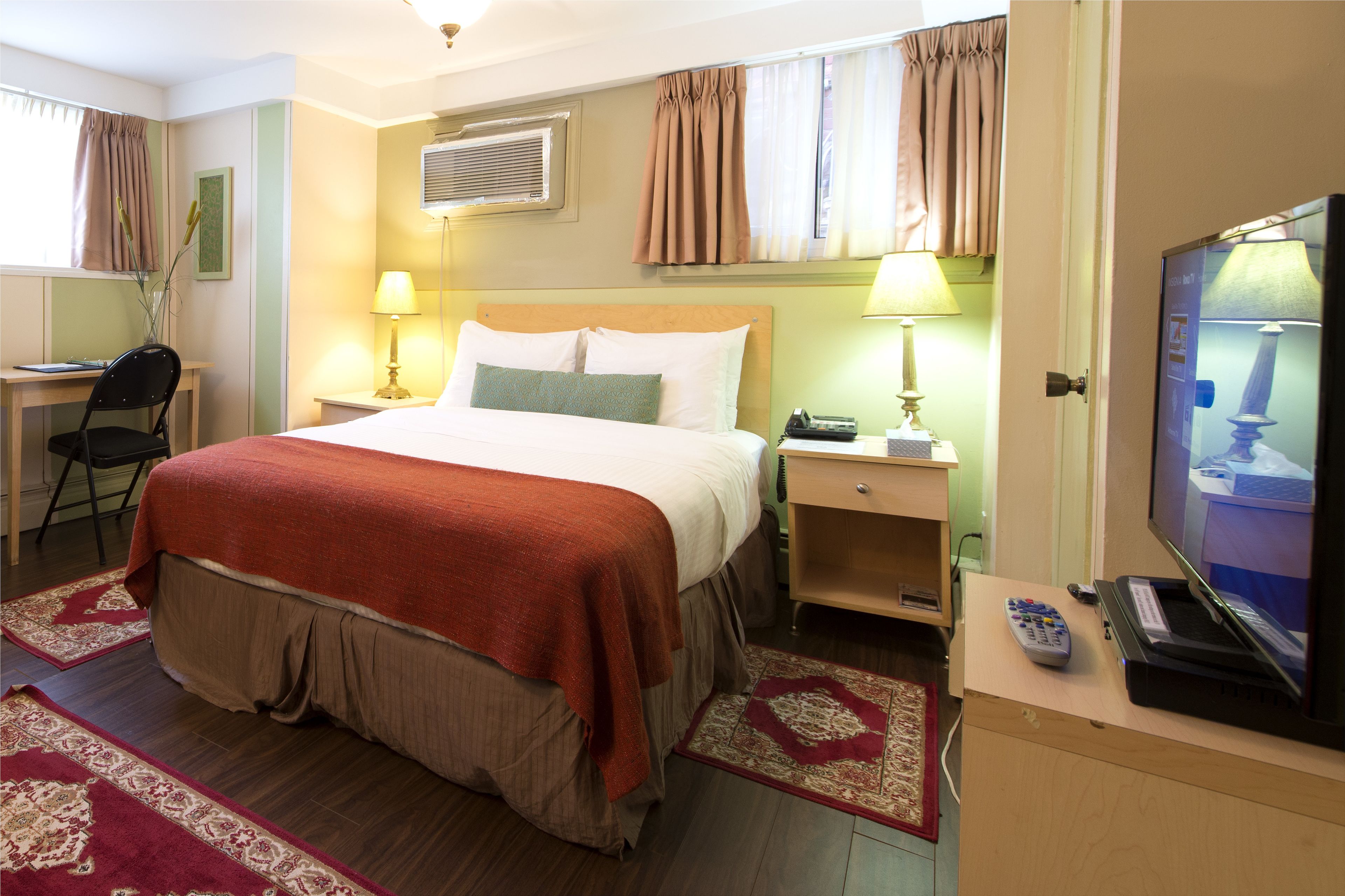 Quarto de hotel com cama, mesas de cabeceira, escrivaninha, cadeira, televisão e janela com cortinas.