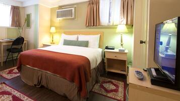 Quarto de hotel com cama, mesas de cabeceira, escrivaninha, cadeira, televisão e janela com cortinas.