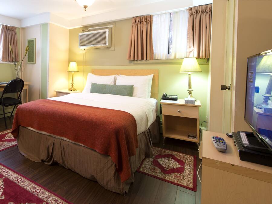 Quarto de hotel com cama, mesas de cabeceira, escrivaninha, cadeira, televisão e janela com cortinas.