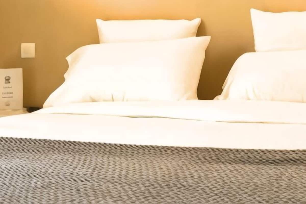 Cama com roupa de cama branca e manta cinza.