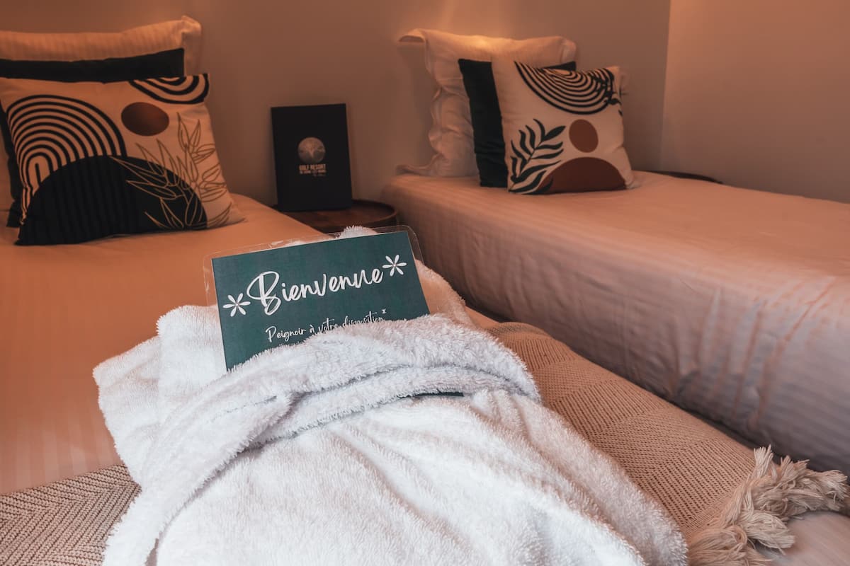 Quarto de hotel com duas camas, um cartão de boas-vindas e luminárias fixadas na parede.