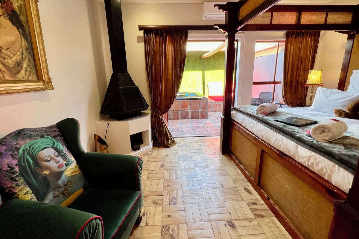 Quarto com cama, sofá, lareira e vista para o exterior.