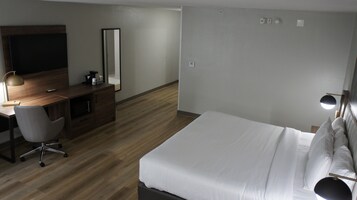 Quarto de hotel com cama, escrivaninha, cadeira, televisão e espelho.