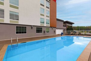 Piscina ao lado de um edifício de hotel com várias janelas e um painel de parede em madeira.
