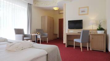 Quarto de hotel com uma cama, uma mesa com um computador, uma televisão e uma cadeira.