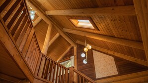Interior em madeira com escada, claraboias e luminárias pendentes.