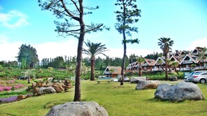 Um resort com vários edifícios em estilo chalé, um gramado bem cuidado com pedras grandes e diversas árvores, incluindo palmeiras e pinheiros.