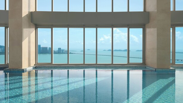 Uma piscina interior ampla com grandes janelas que oferecem vista para uma ponte e horizonte urbano distante.