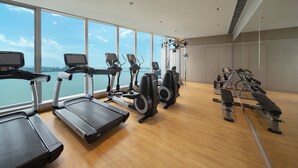 Academia moderna com esteiras, elípticos e equipamentos de musculação, com amplas janelas e vista para a cidade.