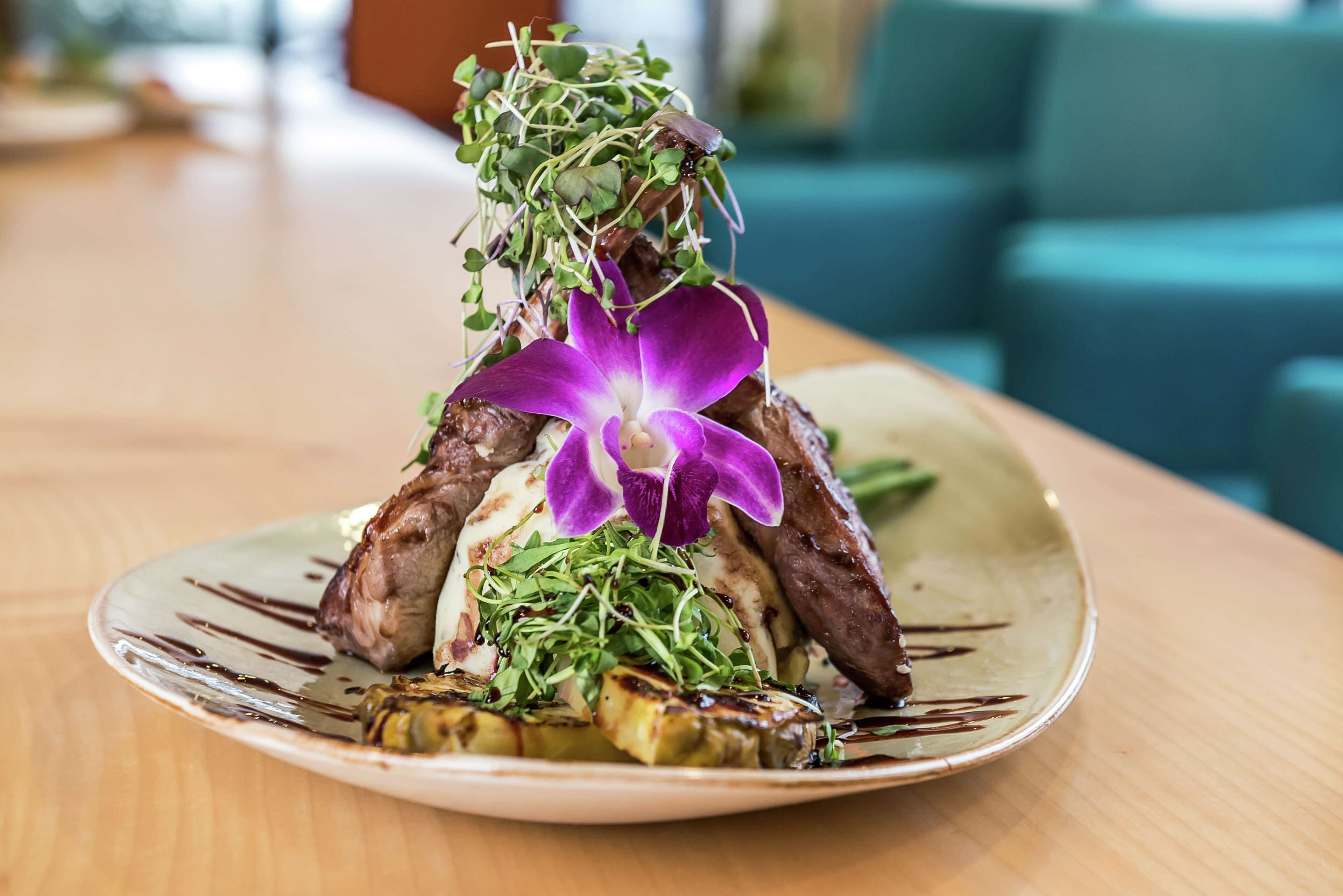 Prato de comida com carne grelhada, legumes e uma flor roxa para decorar.