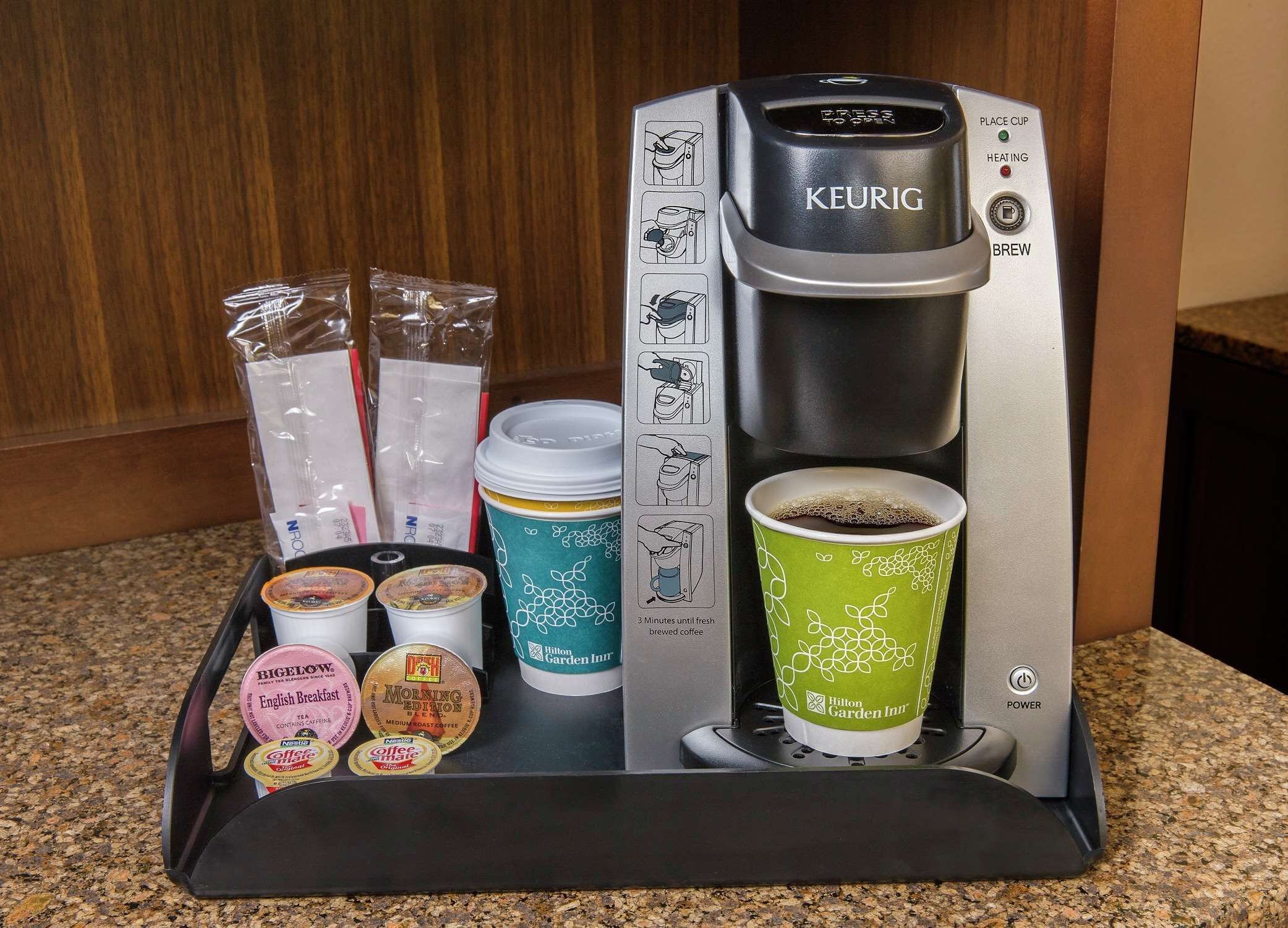 Uma cafeteira Keurig com uma xícara de café e diversos sachês de café em uma bancada.
