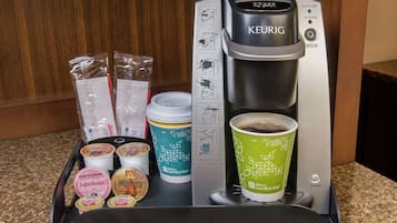 Uma cafeteira Keurig com uma xícara de café e diversos sachês de café em uma bancada.