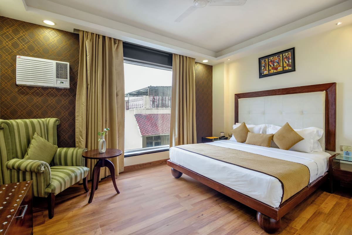 Quarto de hotel com uma cama grande, uma cadeira, uma mesa pequena e uma janela com cortinas.