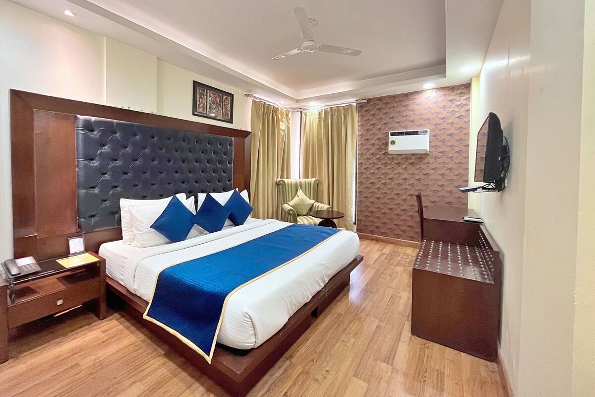 Quarto de hotel com uma cama grande, uma escrivaninha, uma cadeira, uma televisão e ar condicionado.