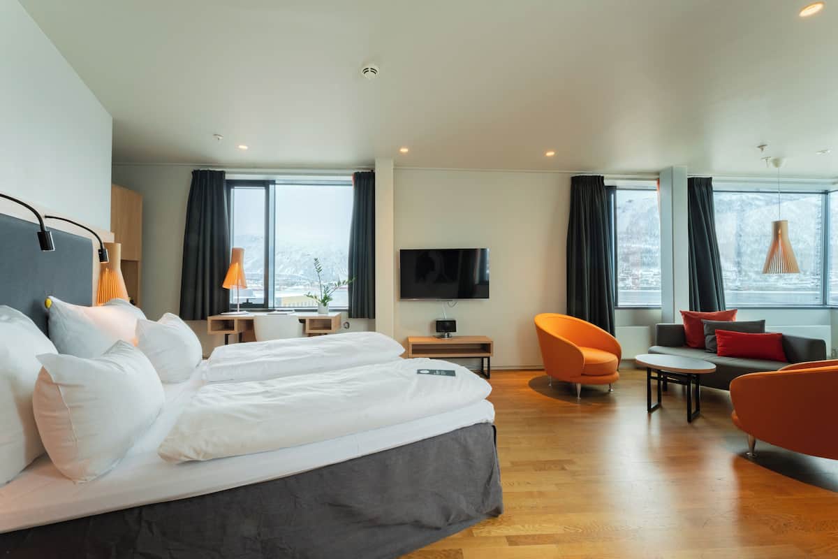 Quarto de hotel moderno com uma cama grande, uma escrivaninha, um sofá e uma televisão.