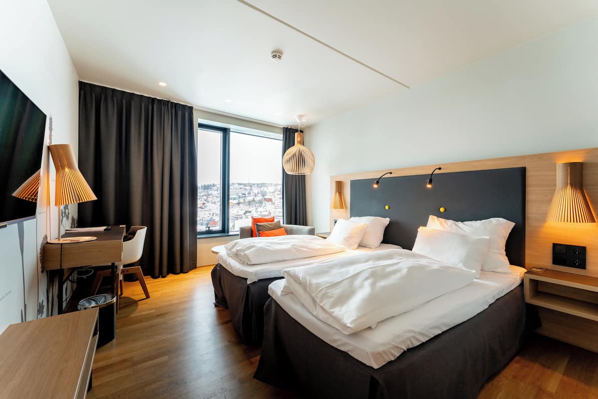 Quarto de hotel moderno com duas camas, uma escrivaninha e uma cadeira.