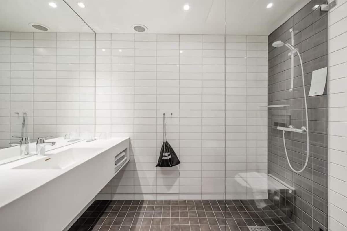 Um banheiro moderno com toucador branco, chuveiro e toalha preta pendurada em um porta-toalhas.
