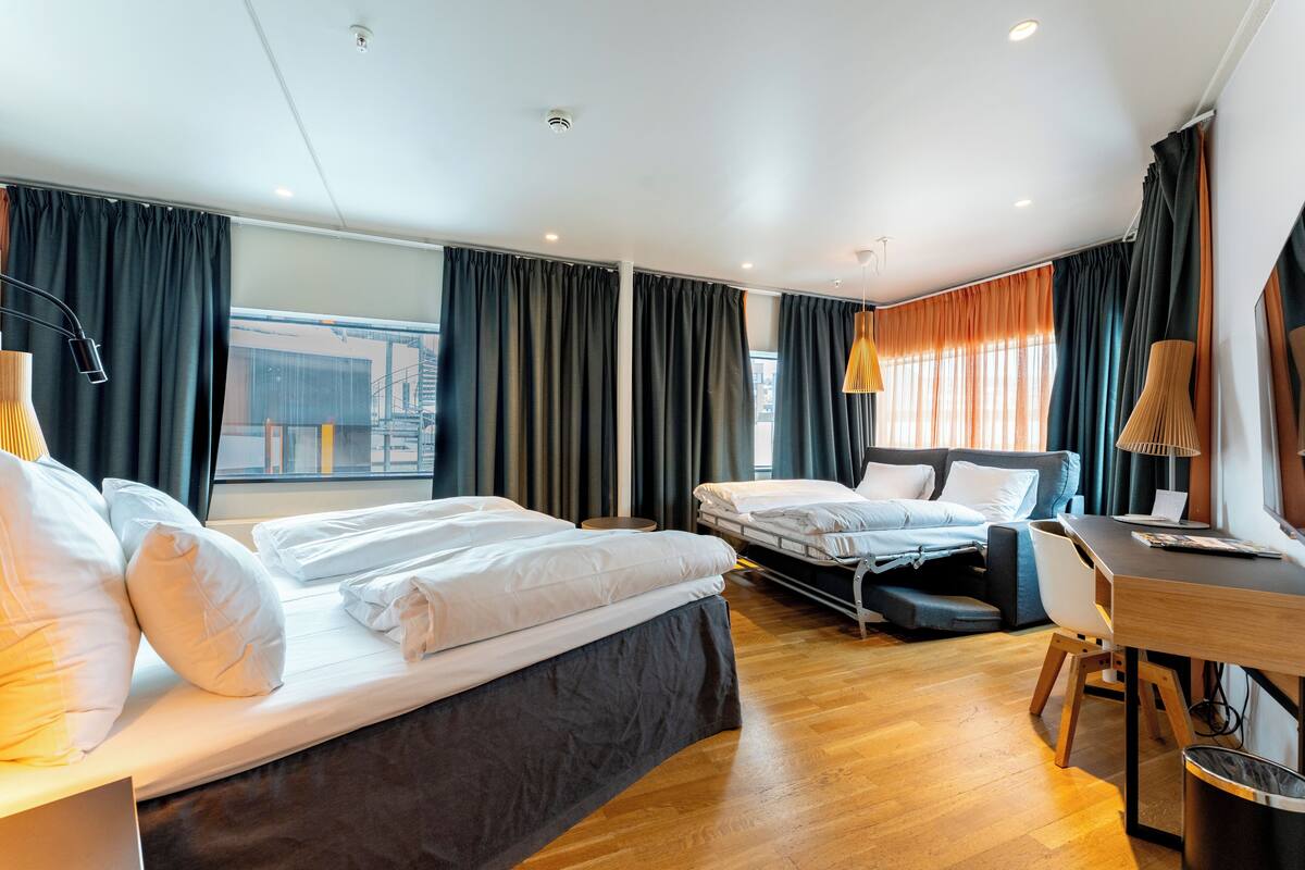 Quarto de hotel moderno com duas camas, uma escrivaninha e uma cadeira.