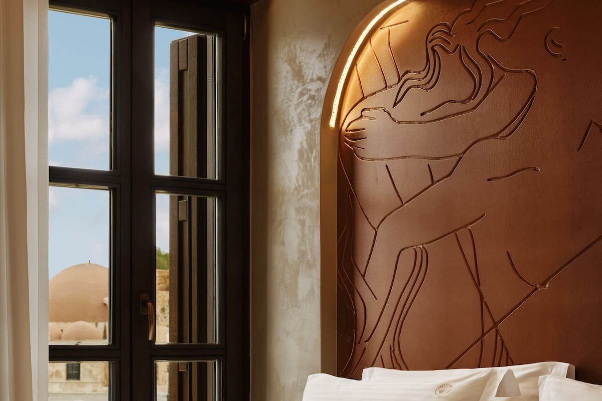 Quarto de hotel com cama, almofadas, vista pela janela e parede com design decorativo.