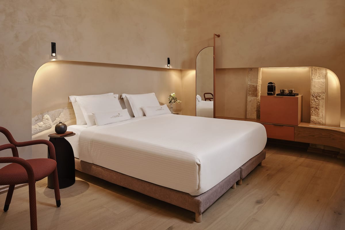 Quarto bem arrumado com cama, mesa de cabeceira, cadeira e espelho.