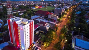 Um hotel imponente, com fachada em vermelho e branco, vários andares e uma área de estacionamento na frente.