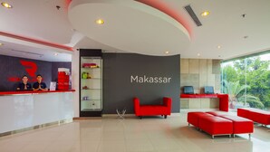 Uma área de recepção moderna, com esquema de cores vermelho e cinza, parede de vidro com vista para o verde e um espaço de estar com sofás vermelhos.
