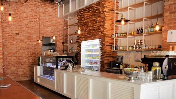 Uma área de bar com parede de tijolos, prateleiras com garrafas e uma geladeira.