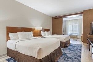 Quarto de hotel com duas camas, uma mesa, uma televisão e uma janela grande.