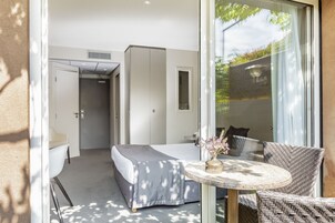 Quarto moderno com cama, uma mesinha com um vaso e uma cadeira de vime.