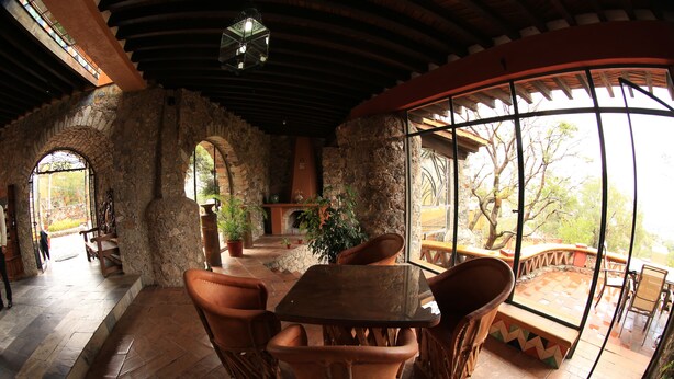 Um pátio externo com cadeiras e mesa de terracota, paredes de pedra e vista para árvores.