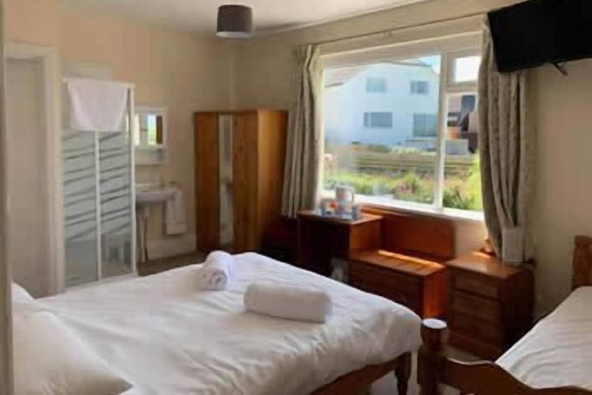 Quarto de hotel com cama, escrivaninha, cadeira, guarda-roupa e janela com vista para edifícios e áreas verdes.