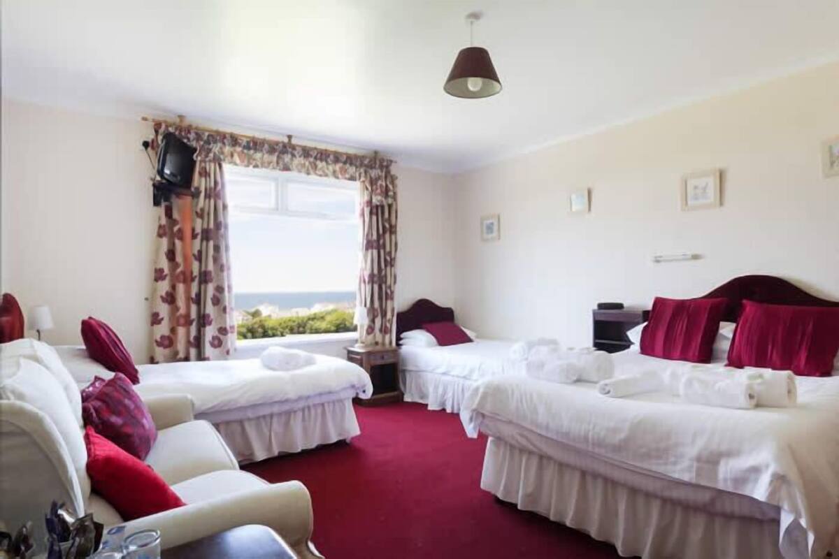 Quarto de hotel com duas camas de solteiro, um sofá, uma mesa e vista para o mar.